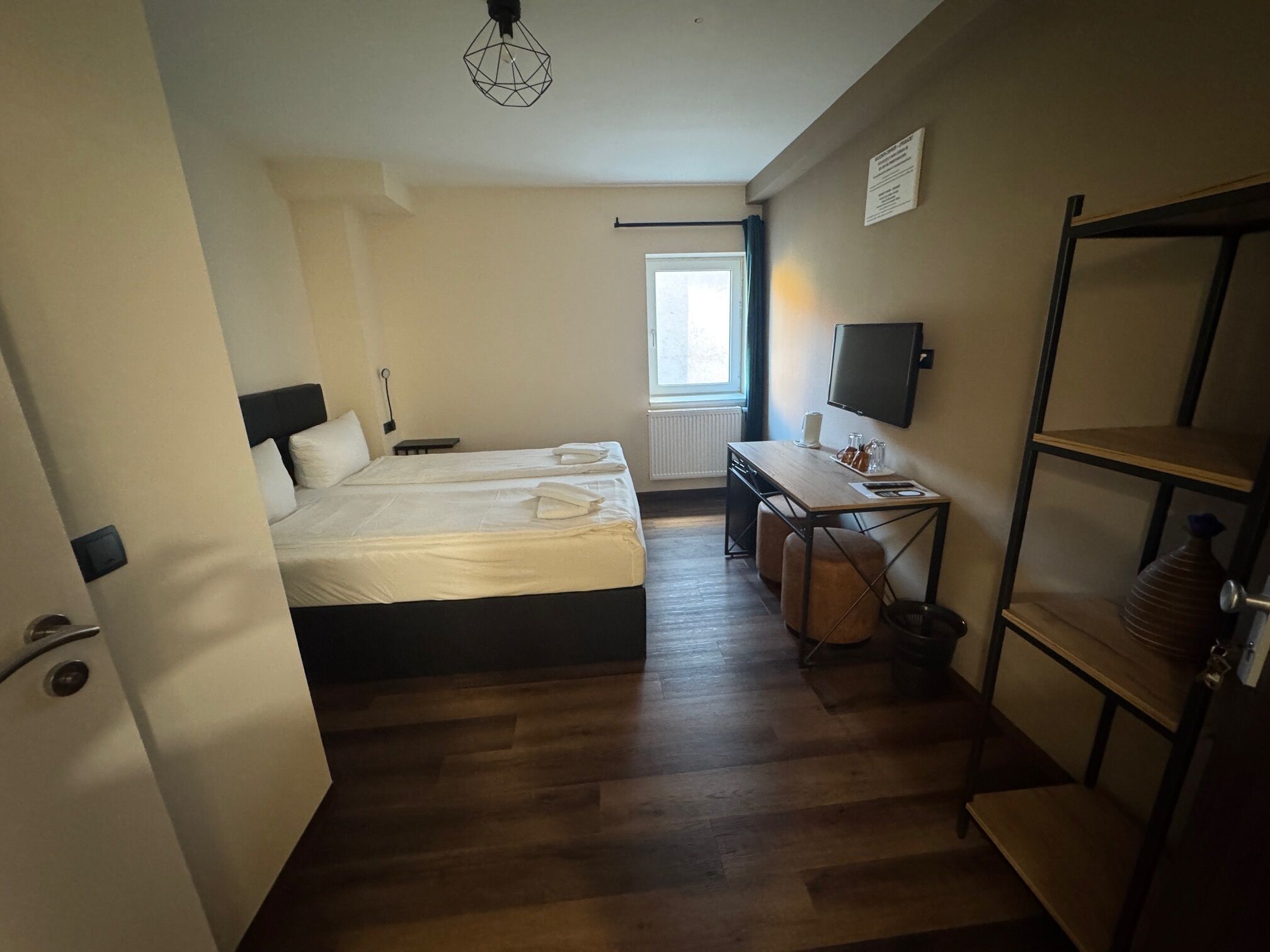 Quarto de hotel compacto com cama, escrivaninha e televisão.