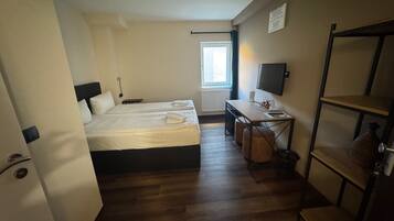 Quarto de hotel compacto com cama, escrivaninha e televisão.