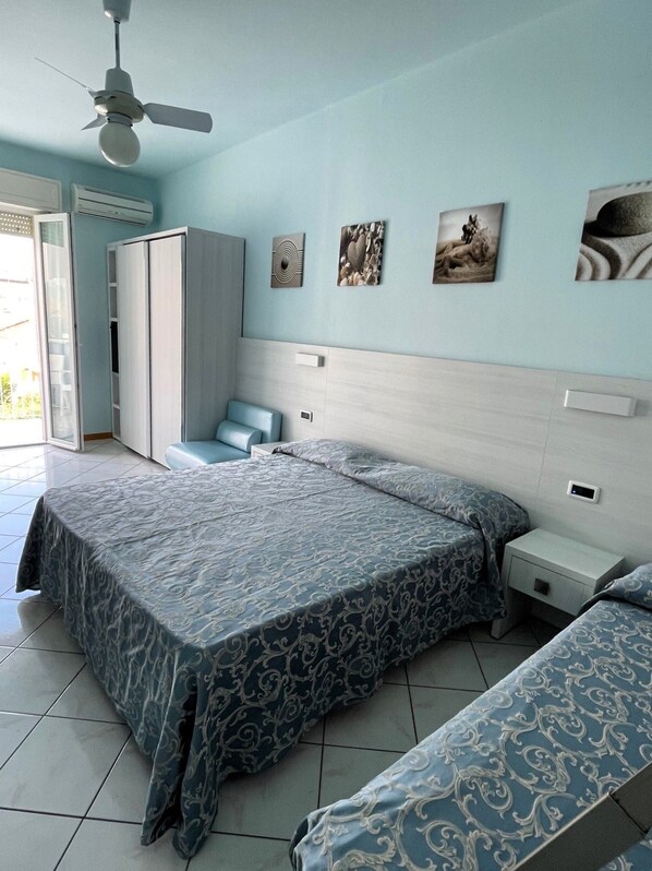 Quarto com cama, mesa de cabeceira, guarda-roupa e ventoinha no teto.