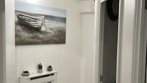 Um corredor com uma porta branca, um console branco com pequenas plantas e um quadro de um barco na parede.
