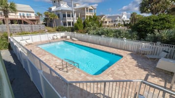 Piscina retangular com deck branco e escada de metal, cercada por uma cerca branca.