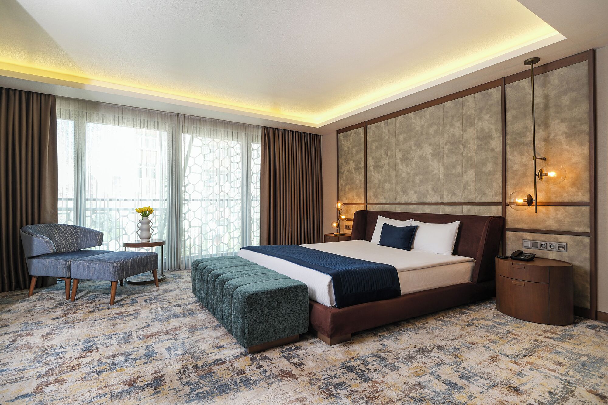 Quarto de hotel com uma cama grande, uma cadeira, uma mesinha e uma criadeira.
