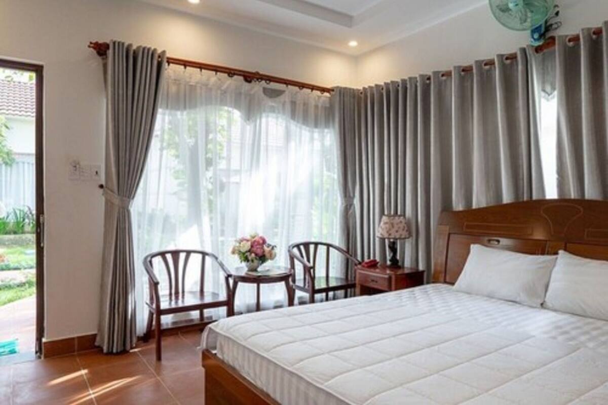 Um quarto com uma cama grande, duas cadeiras, uma mesa pequena com abajur e cortinas.