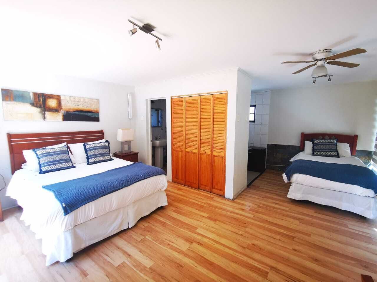 Quarto com duas camas, piso de madeira, guarda-roupa e ventoinha no teto.