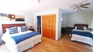 Quarto com duas camas, piso de madeira, guarda-roupa e ventoinha no teto.