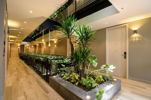 Corredor de hotel com um arranjo de plantas, piso de madeira e uma escada.