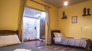 Quarto de hotel com duas camas, porta de correr para uma varanda, ventilador de teto e ar condicionado fixado na parede.