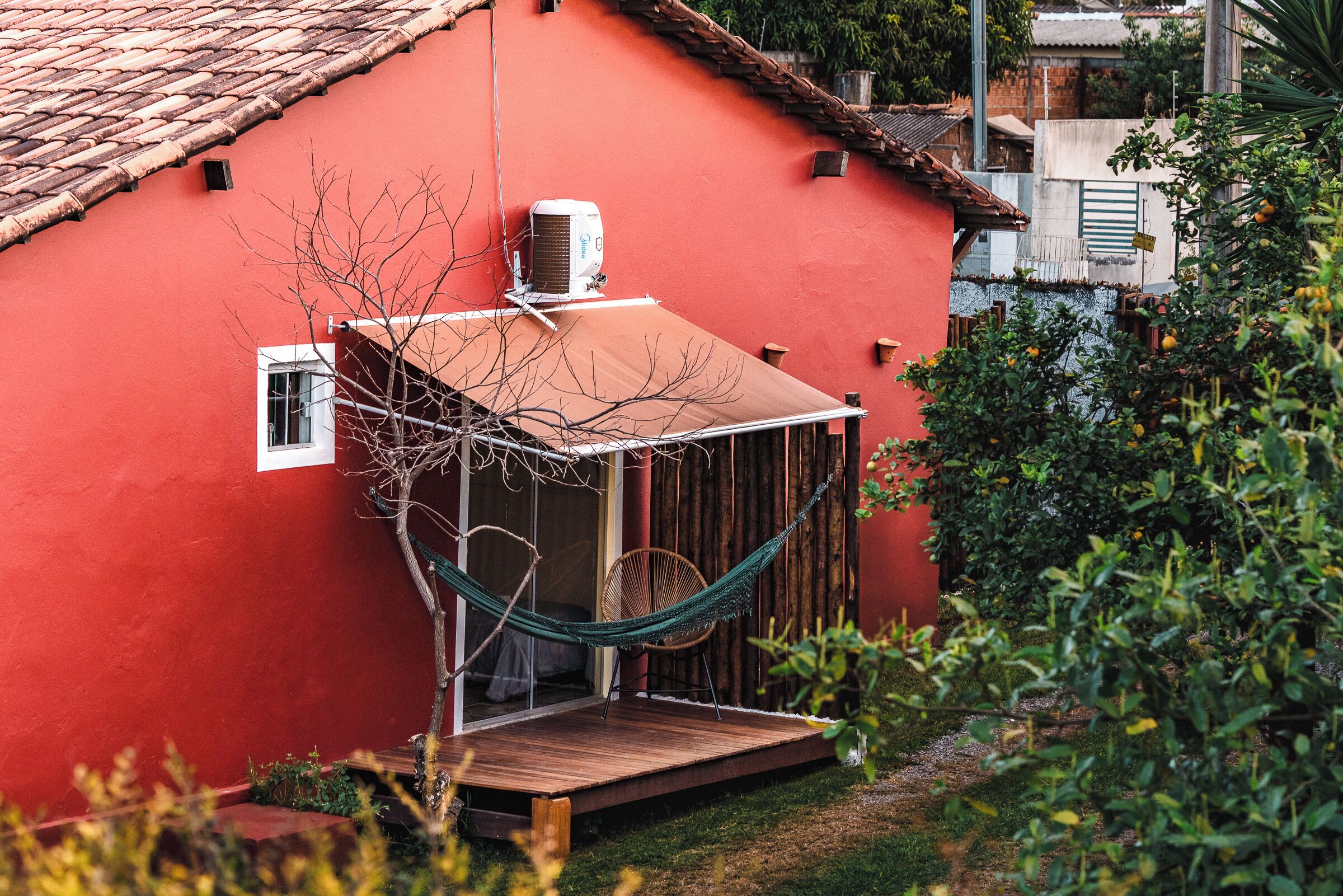 Uma casa vermelha com um deck de madeira, uma rede e uma janela.