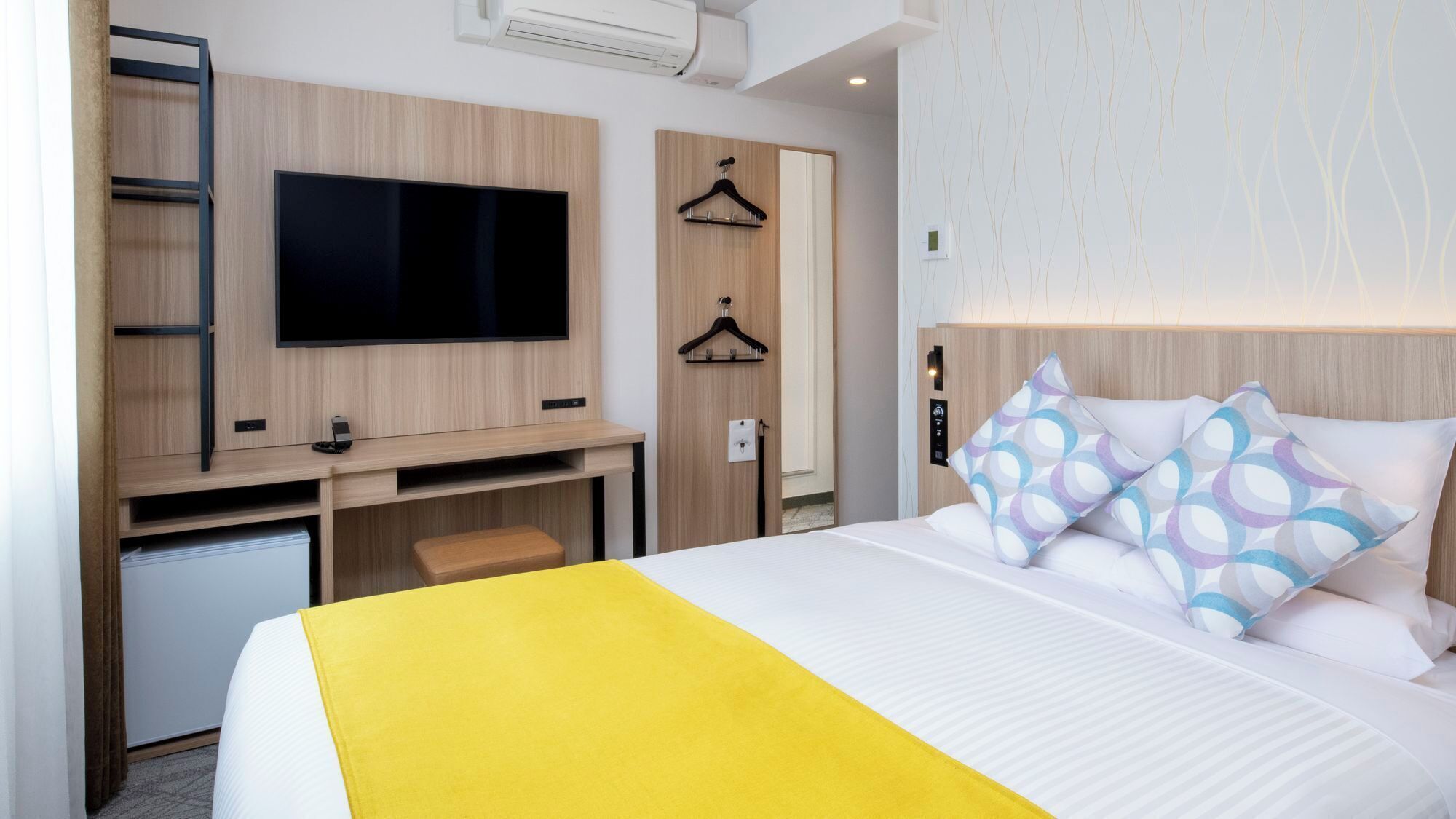 Quarto de hotel com cama, televisão, escrivaninha e guarda-roupa.
