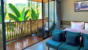 Quarto com cama, sofá, mesa pequena e varanda com grades de madeira e plantas.