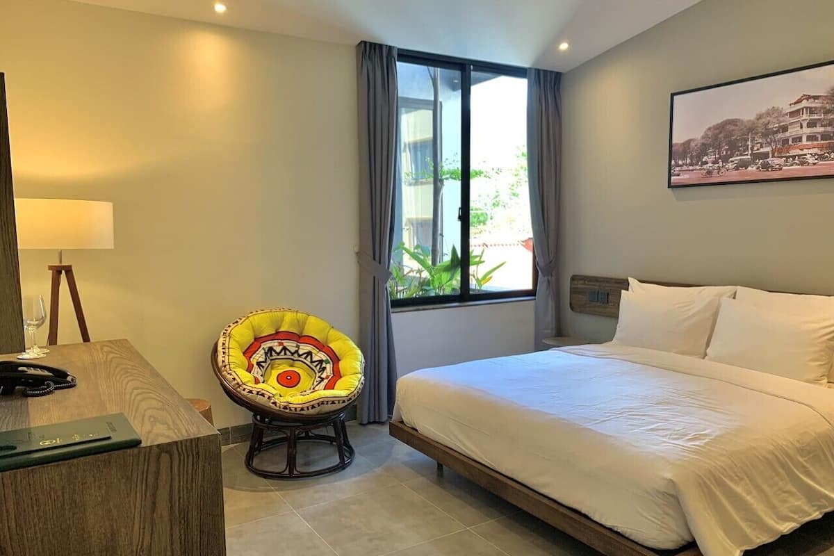 Quarto de hotel com cama, escrivaninha, cadeira e janela com cortinas.