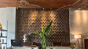 Uma área de recepção com design moderno, destacando uma parede de ripas de madeira, uma planta central e um espaço de estar com mesas e cadeiras.