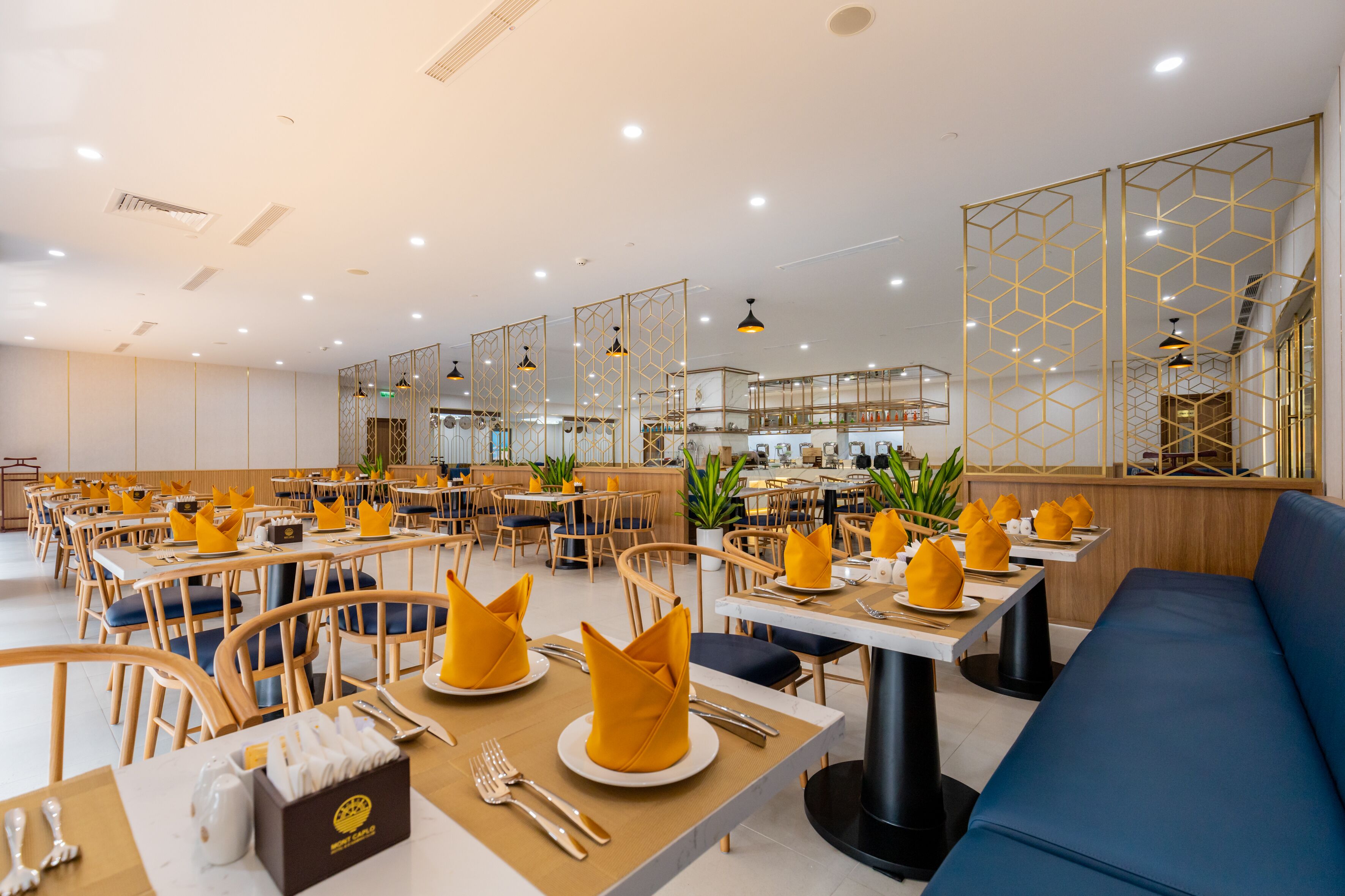 Um restaurante moderno com várias mesas, cada uma com guardanapos amarelos, pratos e talheres.