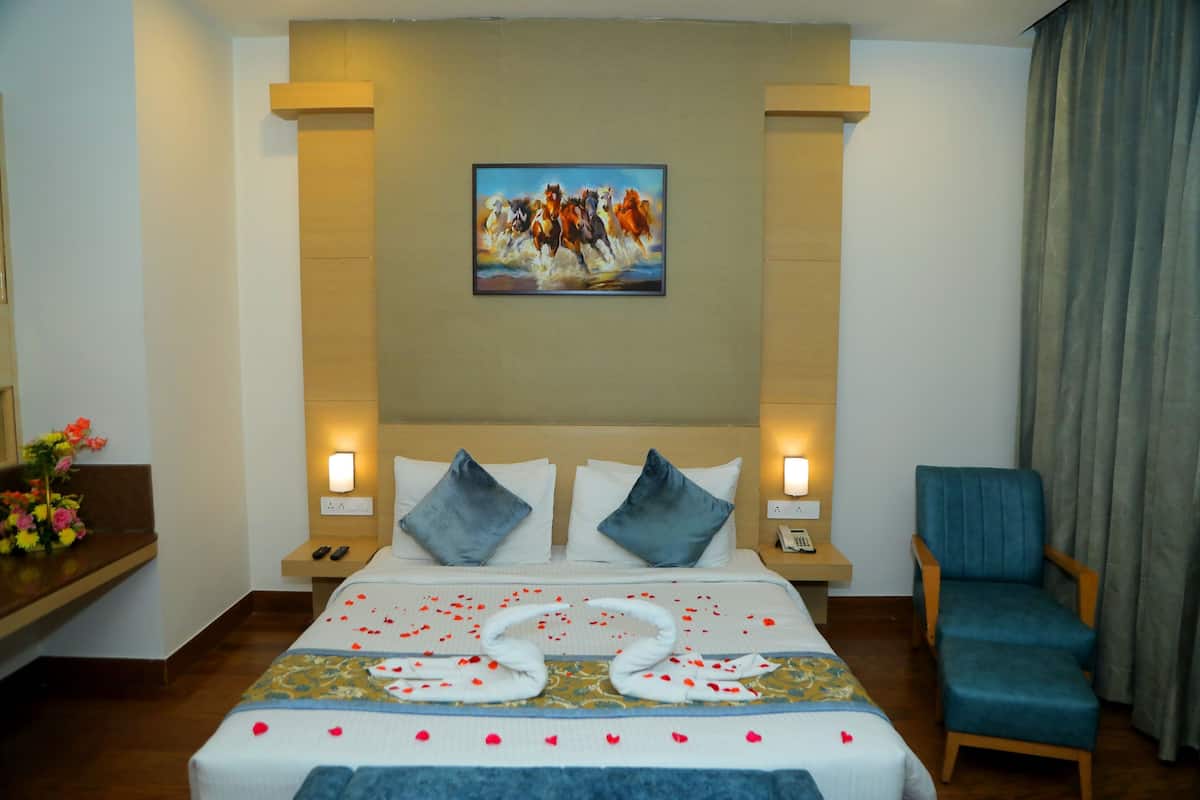 Quarto de hotel com cama, duas mesas de cabeceira, uma cadeira, um quadro na parede e um arranjo floral do lado esquerdo.
