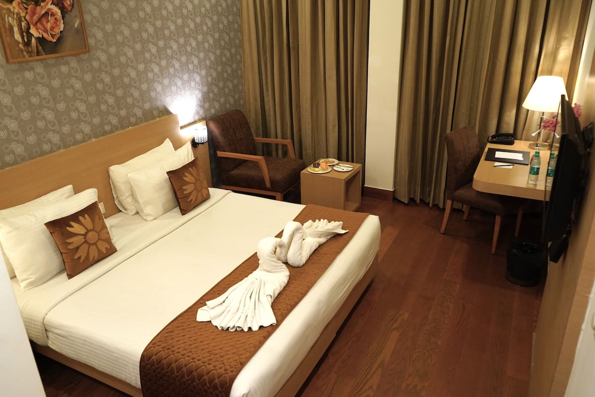 Quarto de hotel com uma cama grande, uma escrivaninha, uma cadeira e uma televisão.