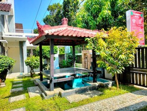 Um gazebo tradicional com telhado de azulejos, uma pequena piscina e um caminho de pedra que leva a ela.