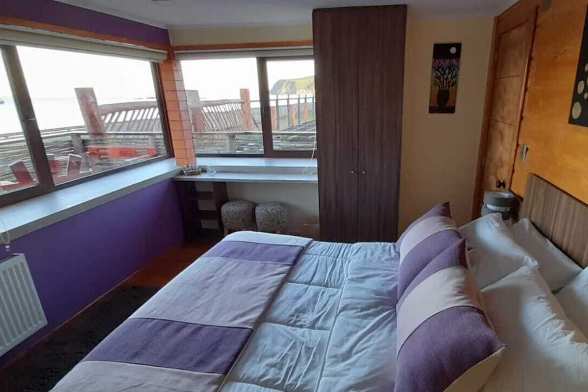 Quarto com cama, janela com vista, radiador e guarda-roupa de madeira.