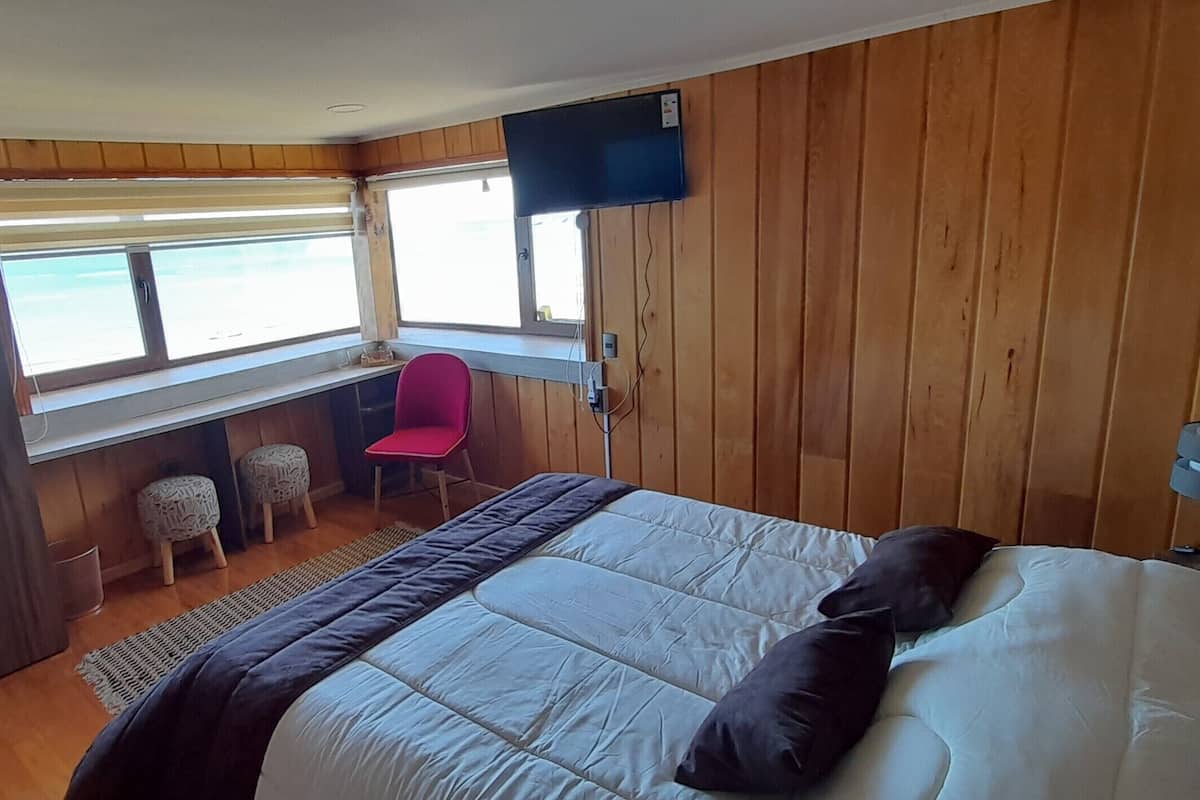 Quarto com cama, escrivaninha, cadeira e televisão.