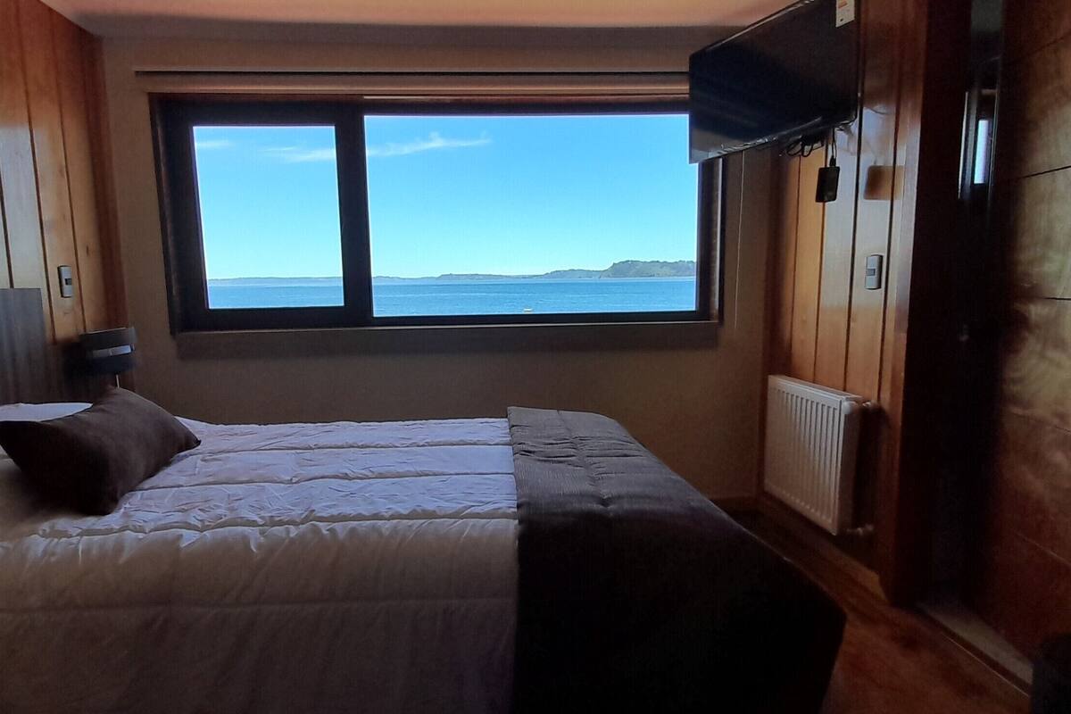 Um quarto com uma cama, uma janela com vista para o mar e paredes de madeira.