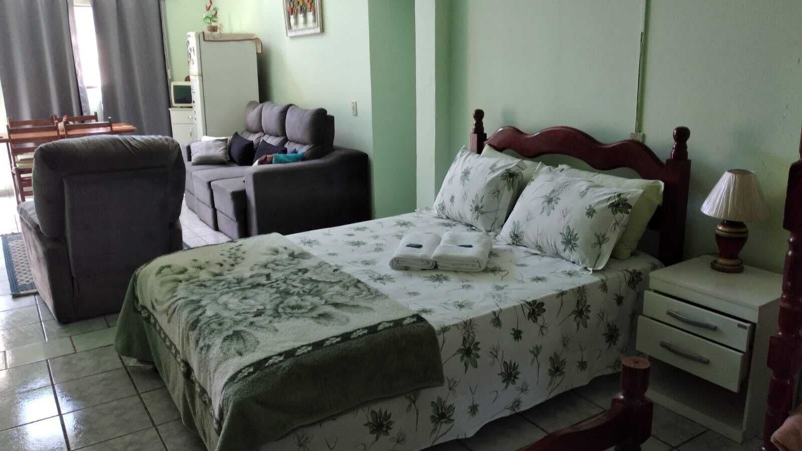 Quarto com cama, poltrona, mesa de cabeceira e cômoda.