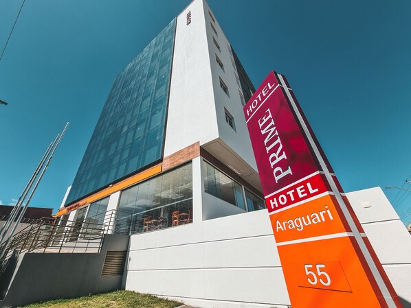 Um hotel moderno com uma fachada de vidro e exterior branco, exibindo uma placa chamativa do Prime Hotel Araguari.