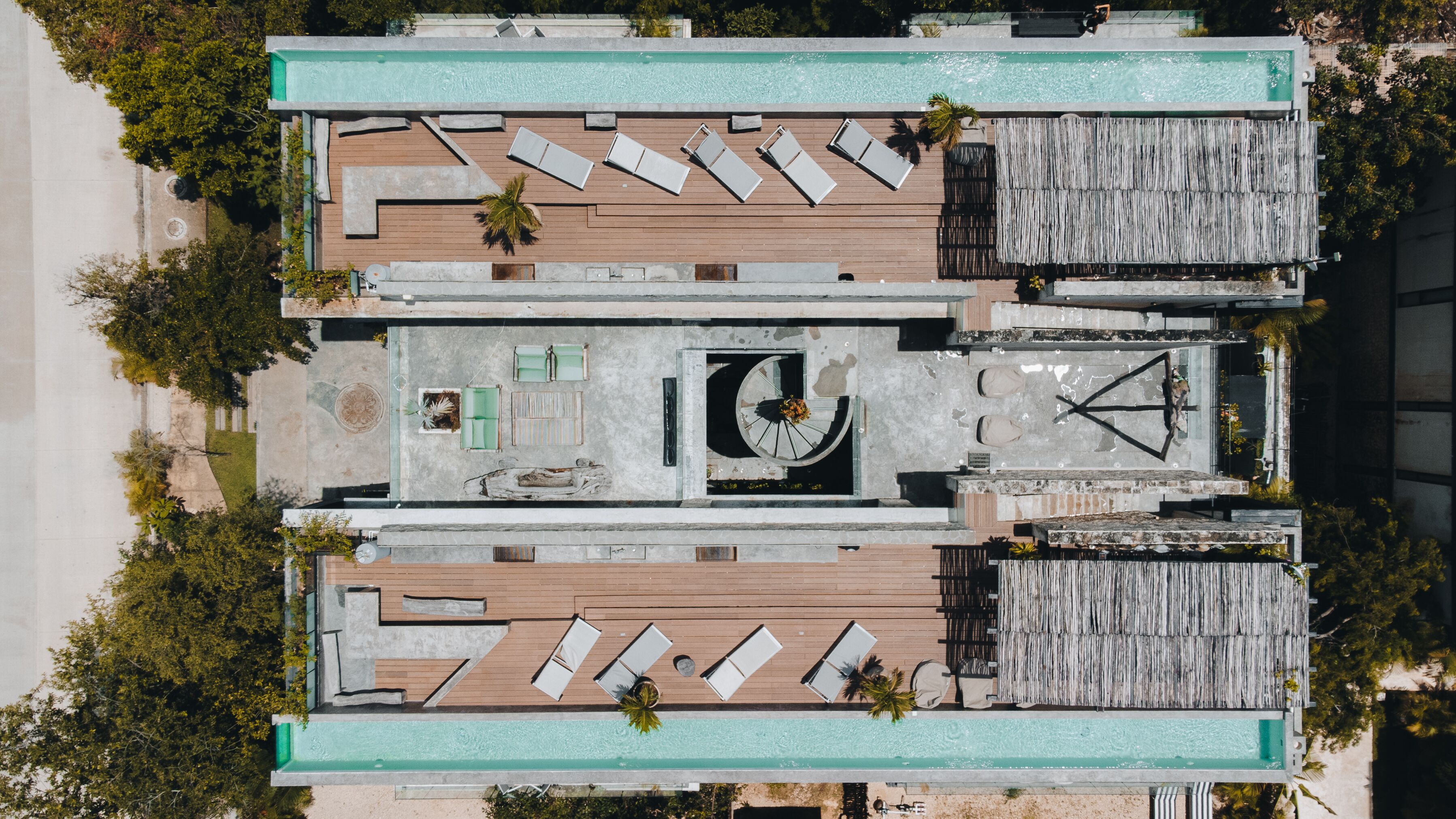 Vista aérea de uma área de piscina no terraço, com várias espreguiçadeiras, um espaço de estar central e uma pequena fonte circular.