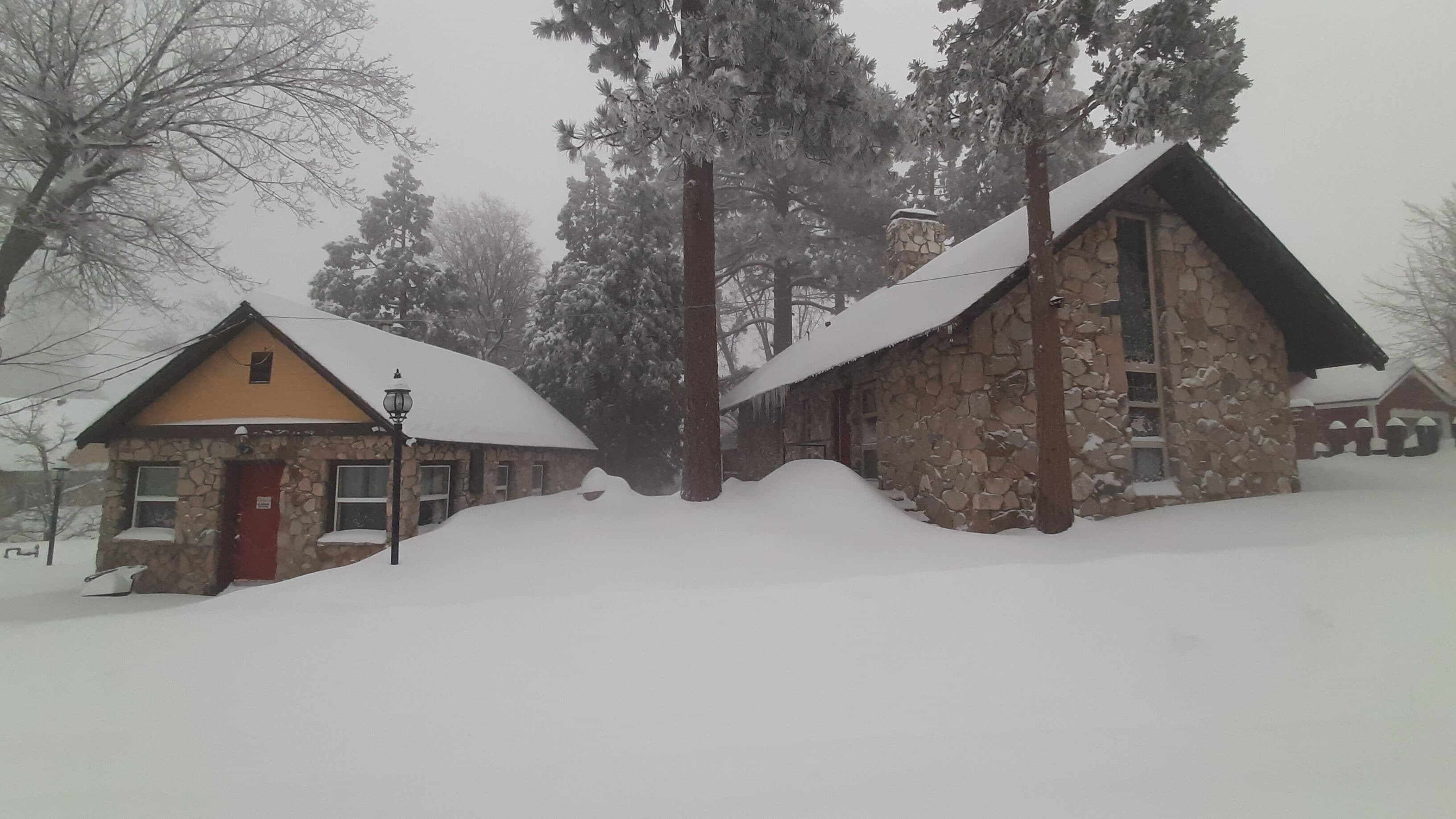 Um edifício de pedra com uma porta vermelha e fachada amarela, rodeado por árvores cobertas de neve.