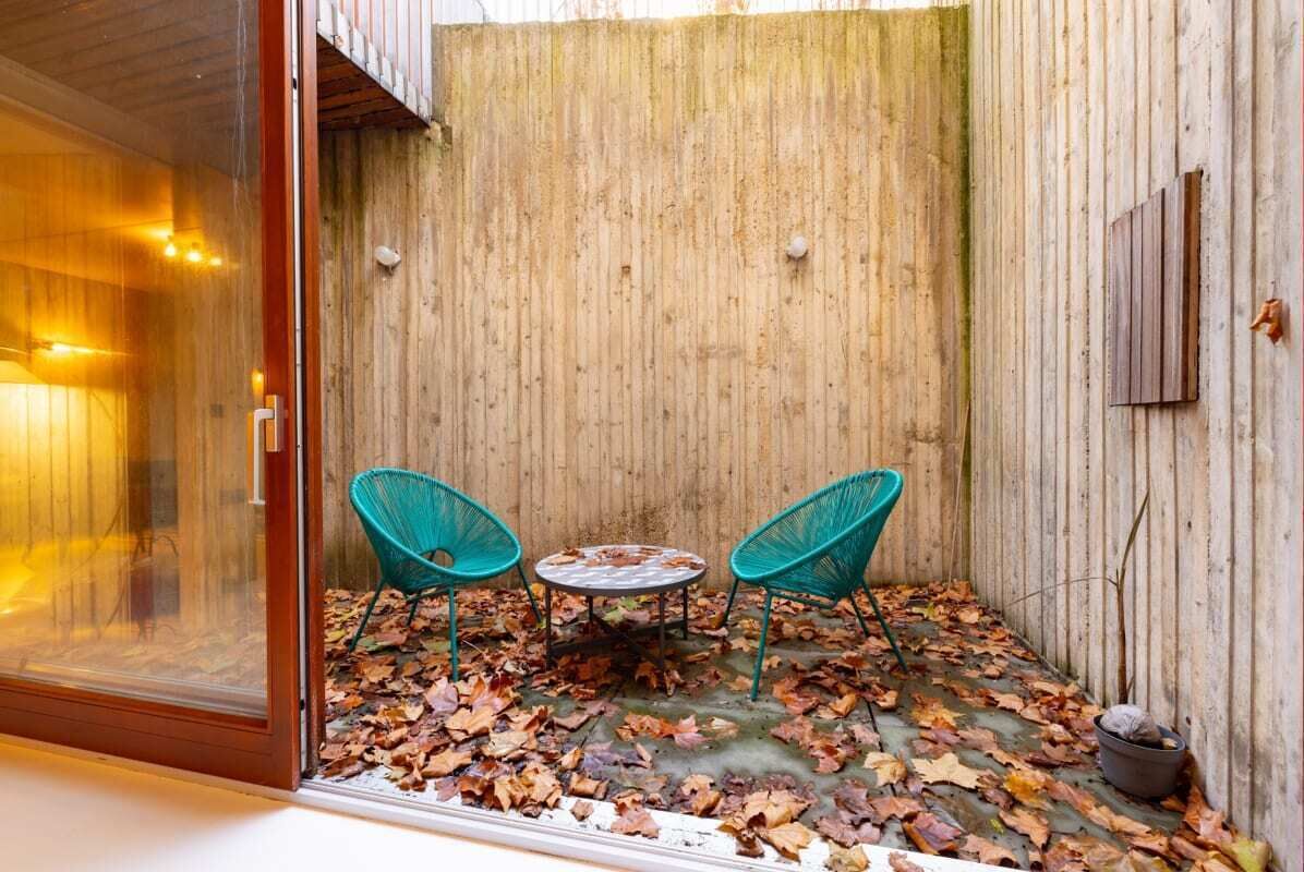 Uma parede de madeira com uma porta de vidro, duas cadeiras verdes e uma mesa pequena.