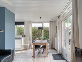 Uma sala de jantar moderna com uma mesa e cadeiras de madeira, uma luminária pendente e vista para um jardim através de janelas amplas.