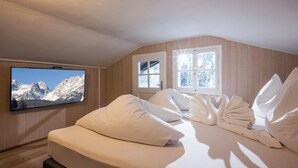Quarto com cama, almofadas, televisão e janelas com vista para a neve.