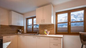 Cozinha moderna com armários brancos, bancada de madeira, cafeteira e janela com vista para as montanhas.