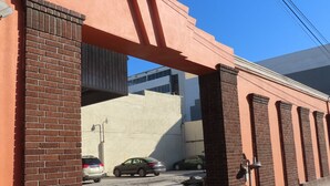 Um edifício com fachada de tijolos e um grande beiral. Carros estão estacionados na frente e uma lixeira é visível.