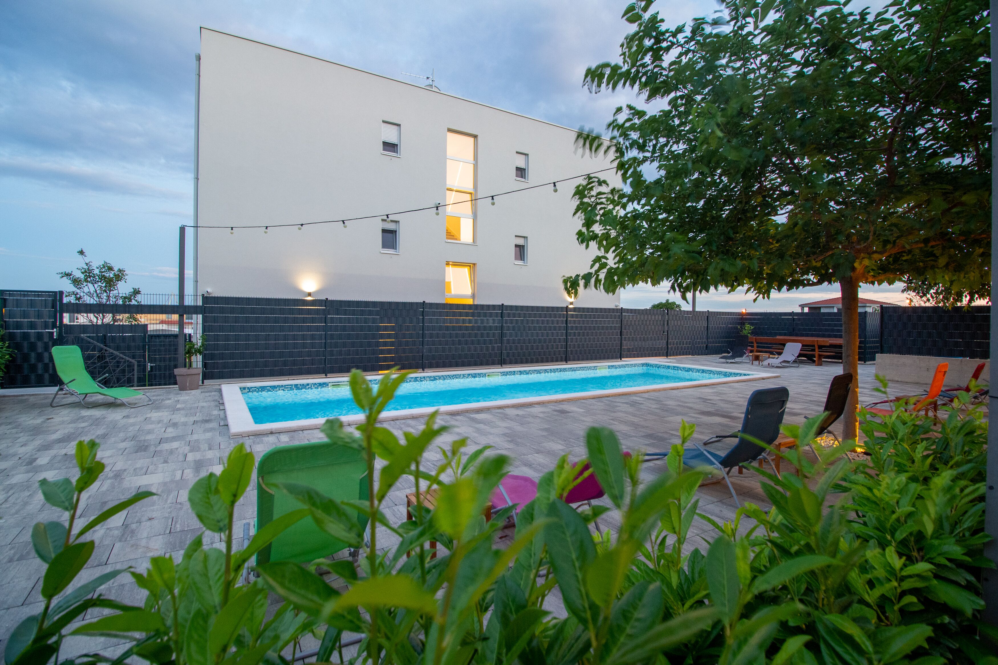 Uma área moderna com piscina ao ar livre, com uma piscina retangular, cercada por espreguiçadeiras e plantas em vasos.