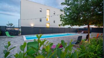 Uma área moderna com piscina ao ar livre, com uma piscina retangular, cercada por espreguiçadeiras e plantas em vasos.