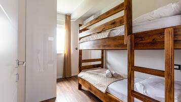 Quarto com beliches de madeira, roupa de cama branca e porta que dá para outro cômodo.