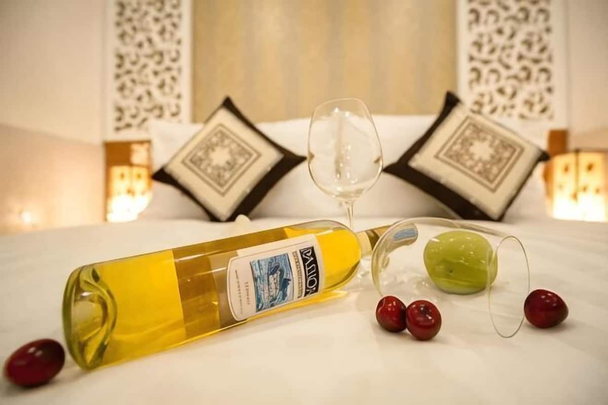 Uma garrafa de bebida alcoólica, um copo e cerejas sobre a cama em um quarto de hotel.