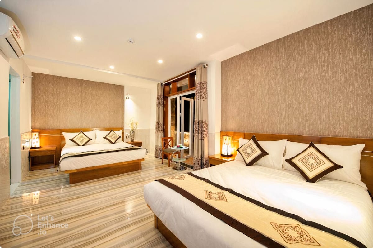 Quarto de hotel com duas camas, área de estar e uma janela grande com cortinas.