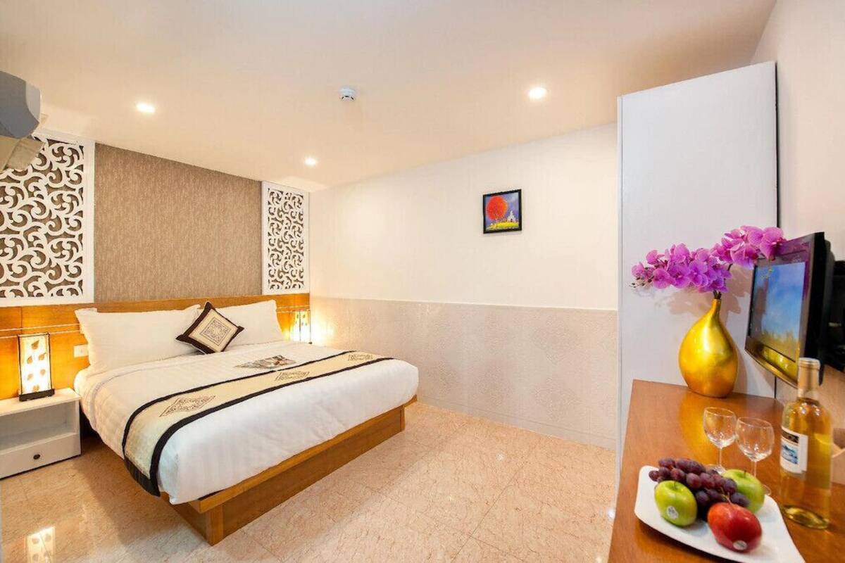 Quarto de hotel com cama, mesa de cabeceira, decoração na parede e uma cesta com frutas e vinho.