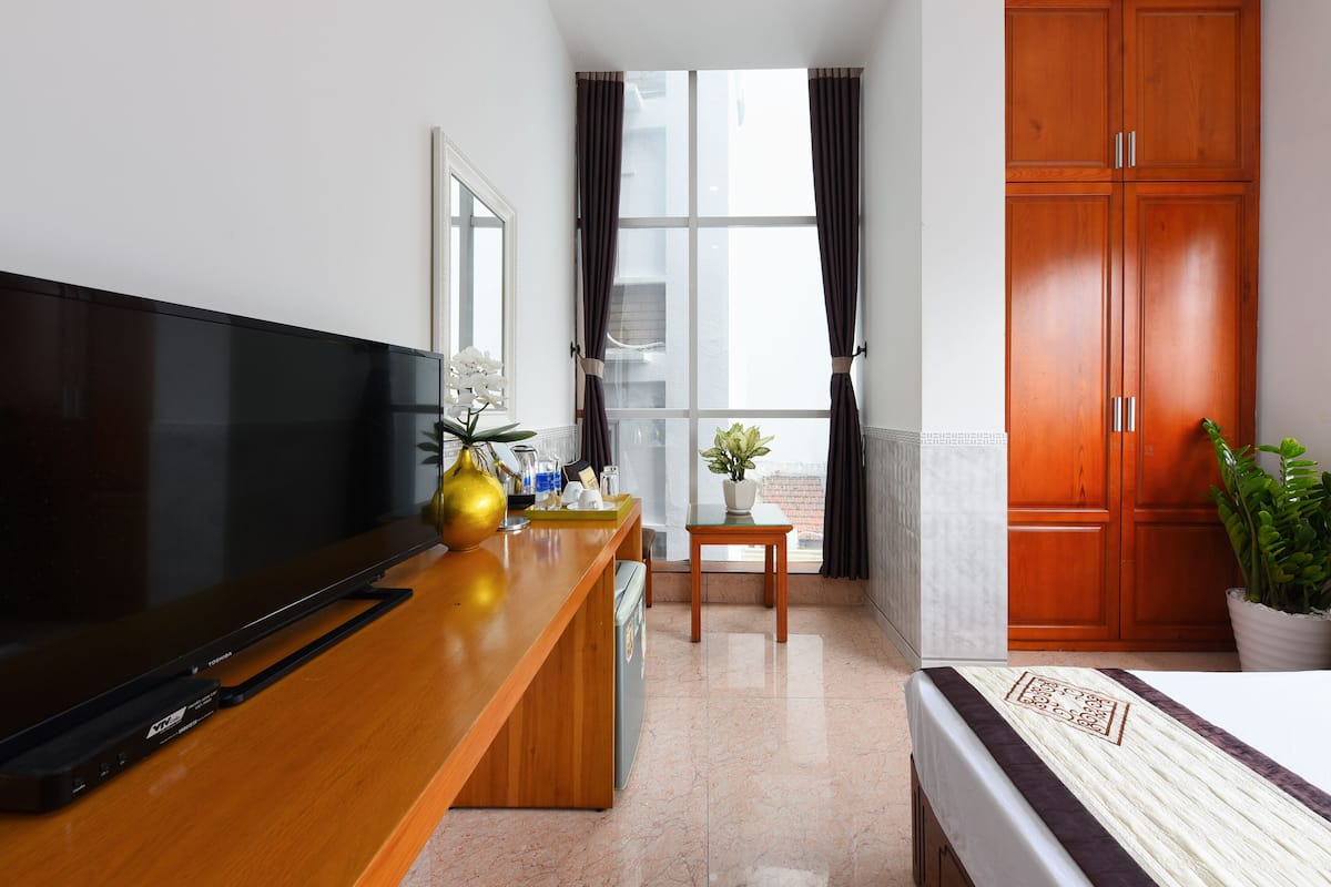 Quarto de hotel com televisão de tela plana, escrivaninha de madeira, plantas em vasos e um guarda-roupa espaçoso.