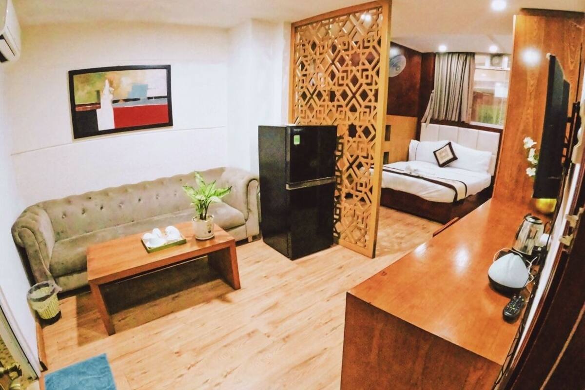 Um espaço de estar compacto com sofá, mesa de centro, TV e pequeno espaço de cozinha.