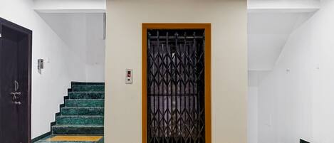 Um corredor com escada que leva a uma porta com grade de metal.
