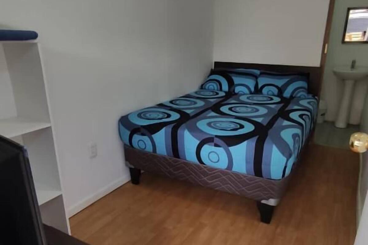 Um quarto pequeno com uma cama, uma escrivaninha e uma televisão.