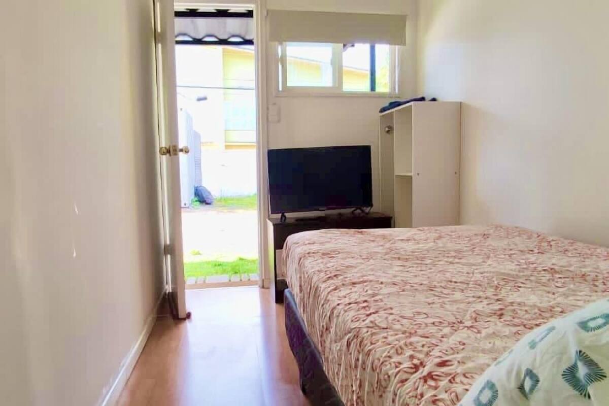 Quarto com cama, televisão e guarda-roupa. Uma porta dá para área externa.