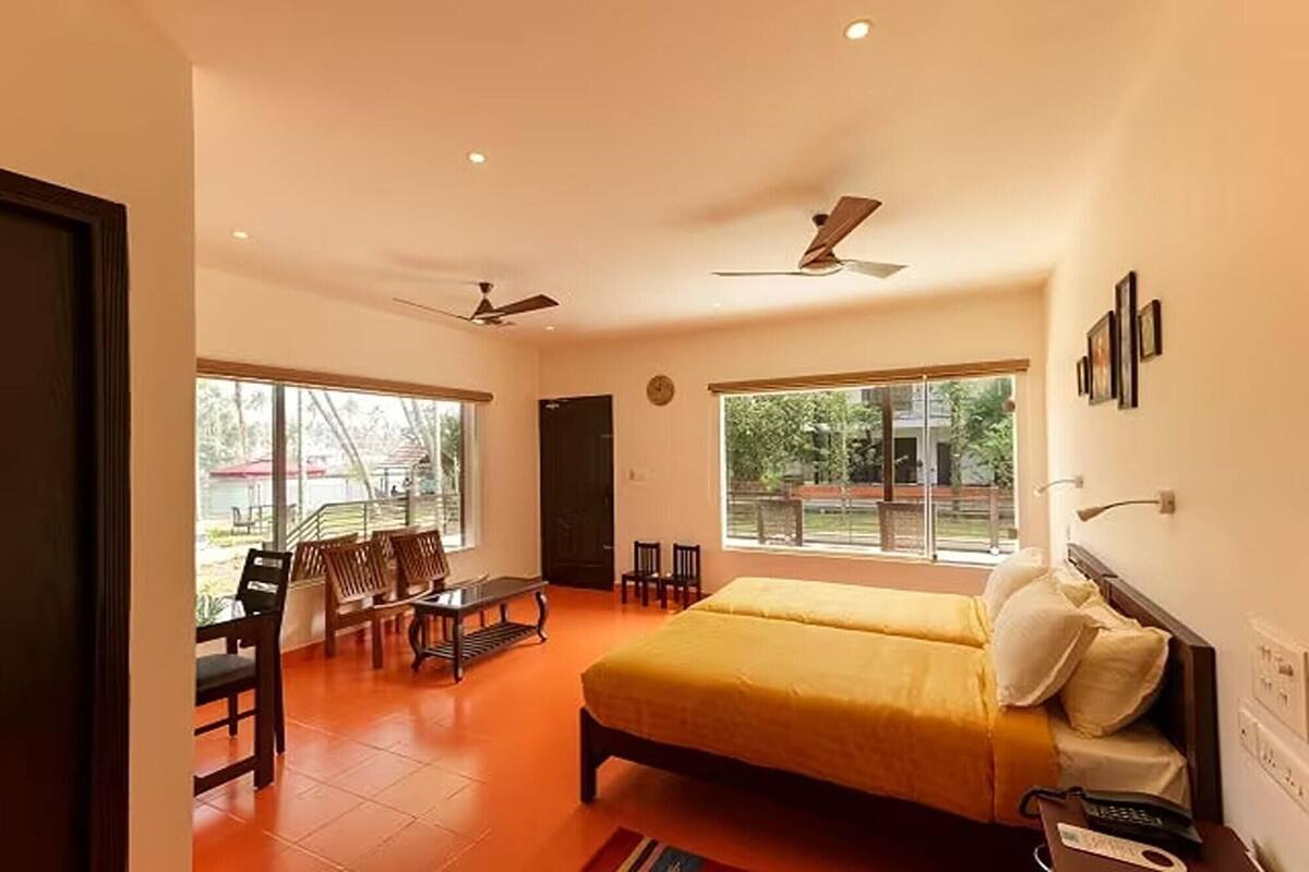 Quarto com cama, escrivaninha, cadeiras, ventilador de teto e grandes janelas.