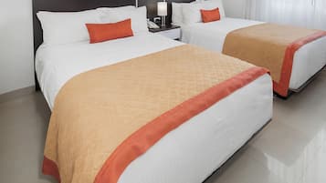 Quarto de hotel com duas camas, cada uma com roupa de cama branca e detalhes em laranja. Há uma mesa de cabeceira com abajur e telefone entre as camas.