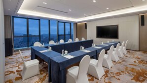 Uma sala de conferências com uma mesa comprida, cadeiras brancas, uma tela grande e vista para a cidade.