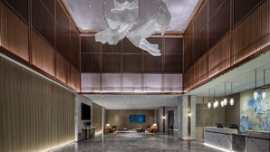 Um hall amplo com balcão de recepção, área de estar e uma grande escultura abstrata.