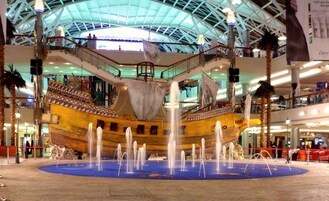 Uma grande fonte interior com uma estrutura em formato de navio no centro, rodeada por uma área circular azul.