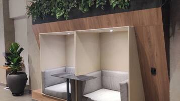Área de estar com bancos acolchoados e uma pequena mesa, cercada por um painel de madeira e um parapeito coberto de plantas.