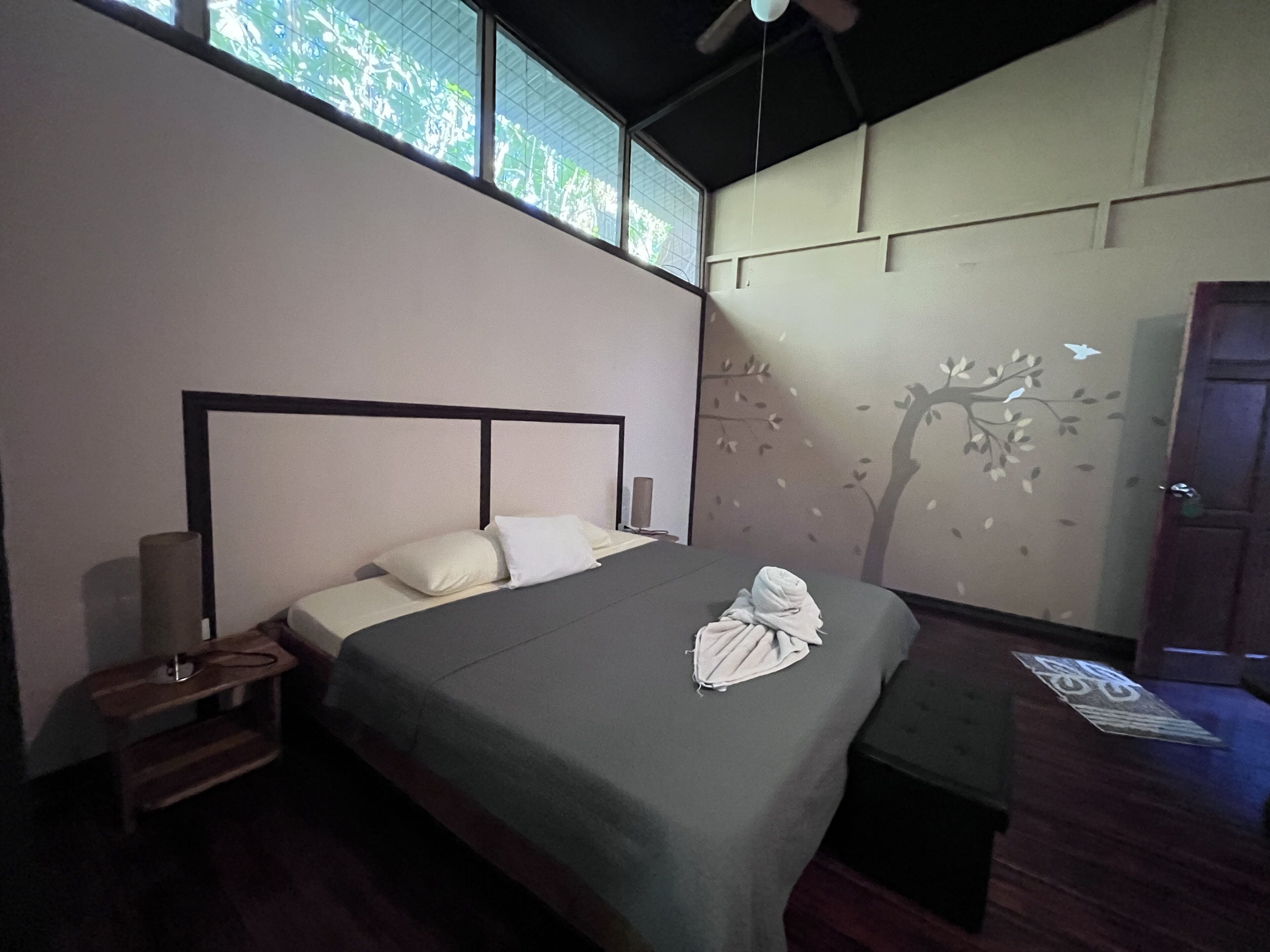 Um quarto com uma cama, mesa de cabeceira e prateleira na parede, além de uma porta.